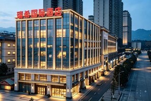Um hotel moderno com fachada de vidro, situado em área urbana com edifícios altos por perto.