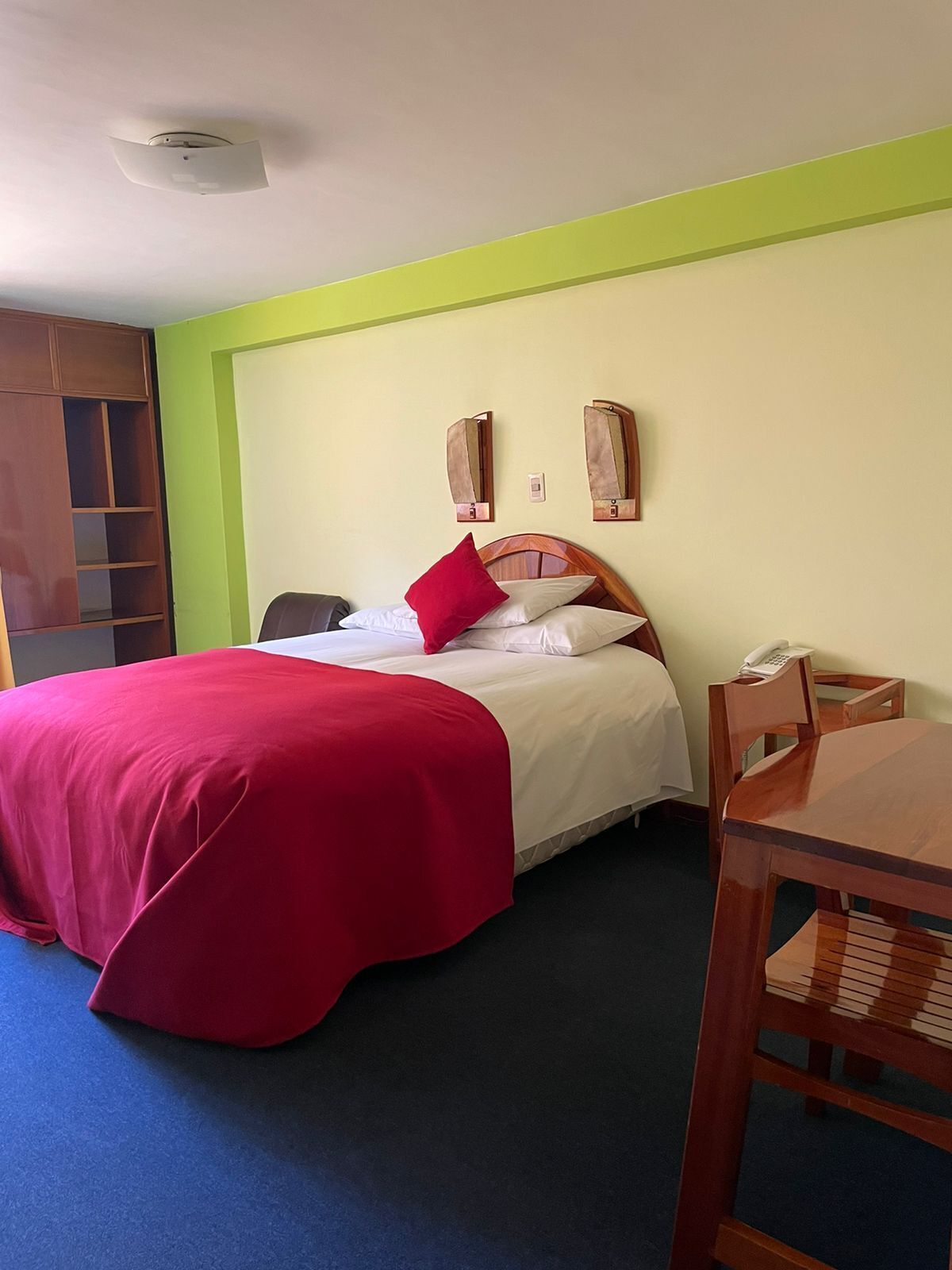 Quarto de hotel com uma cama, uma escrivaninha e uma cadeira.