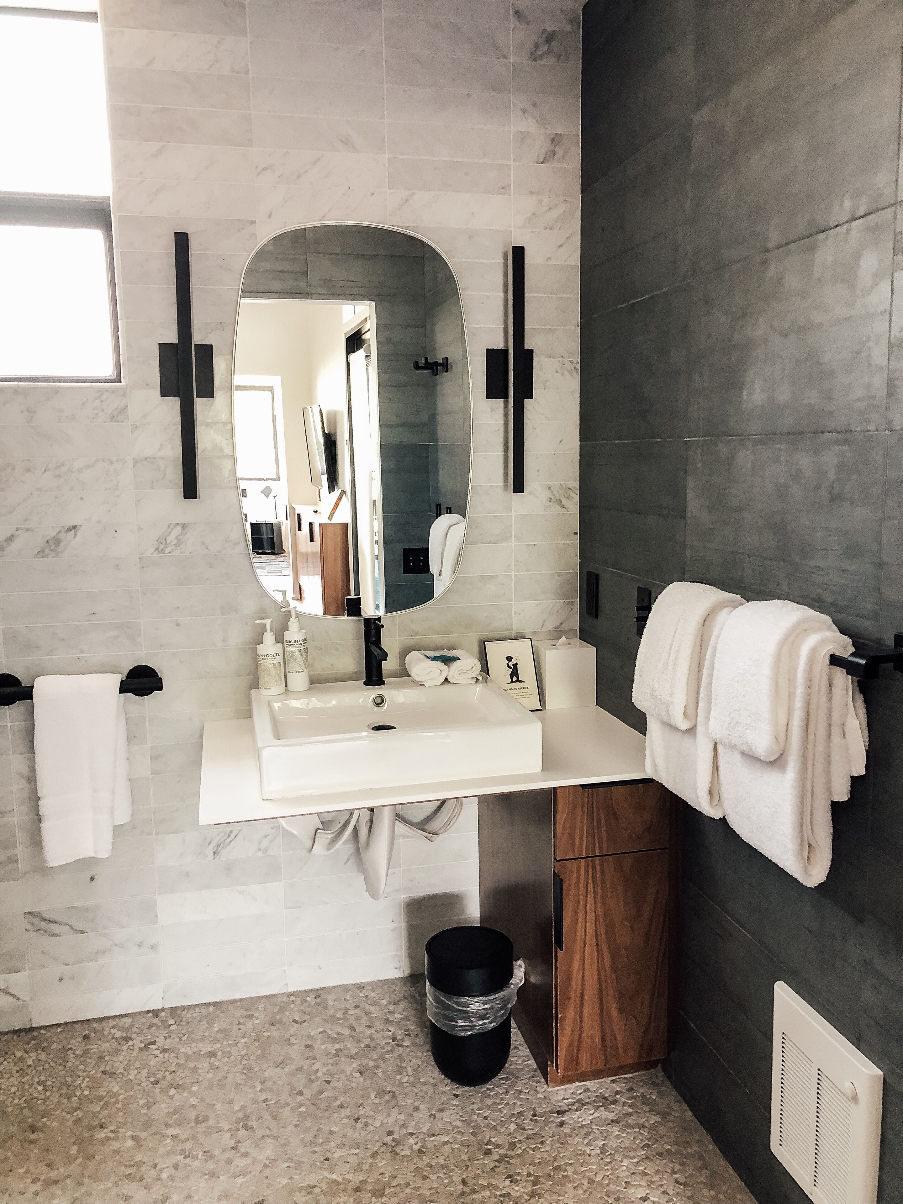 Uma casa de banho moderna com um espelho grande, lavatório branco e duas barras de toalhas.
