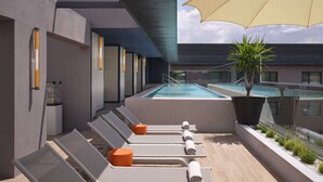 Área de piscina no terraço com espreguiçadeiras, um grande guarda-sol e um vaso de planta.