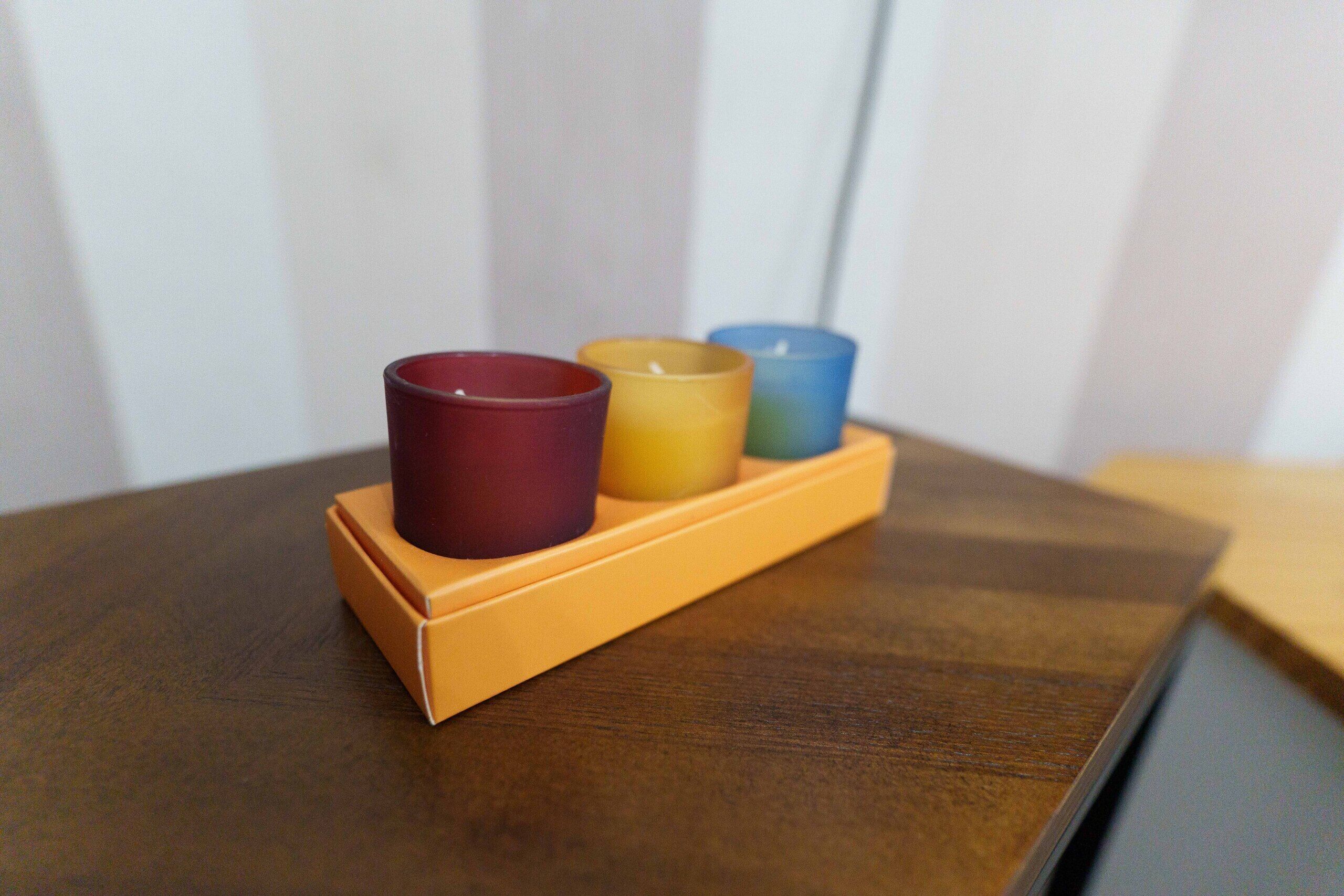 Uma mesa de madeira com uma bandeja que segura três velas em vermelho, amarelo e azul.