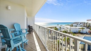 Varanda com cadeiras azuis e vista para a praia e edifícios.