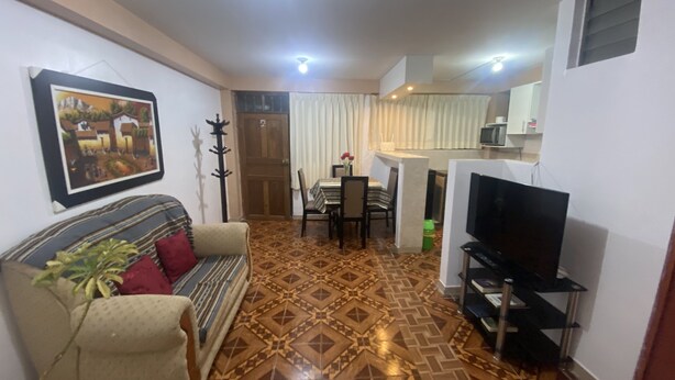 Uma sala de estar com sofá, mesa de jantar com cadeiras, televisão e piso estampado.