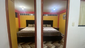 Vista refletida de um quarto com cama, mesas de cabeceira e uma luminária no teto.