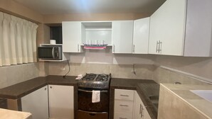 Uma cozinha compacta com fogão a gás, micro-ondas e armários brancos.