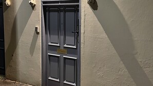 Uma porta escura com uma placa, emoldurada por uma janela em arco, sobre uma parede texturizada.