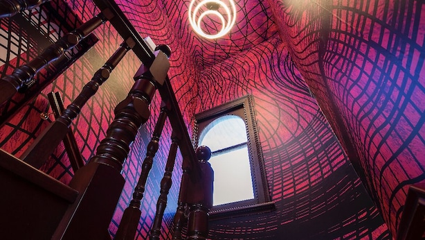 Escada em espiral com vista para o céu através de uma janela, emoldurada por uma parede com padrão vermelho.