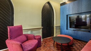 Uma área de estar moderna com uma televisão grande, um sofá vermelho e uma parede estampada.