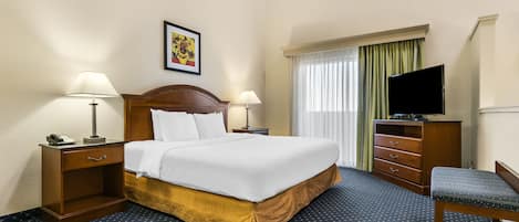 Quarto de hotel com uma cama grande, duas mesas de cabeceira com luminárias, uma TV, um aparador de madeira e uma cadeira.