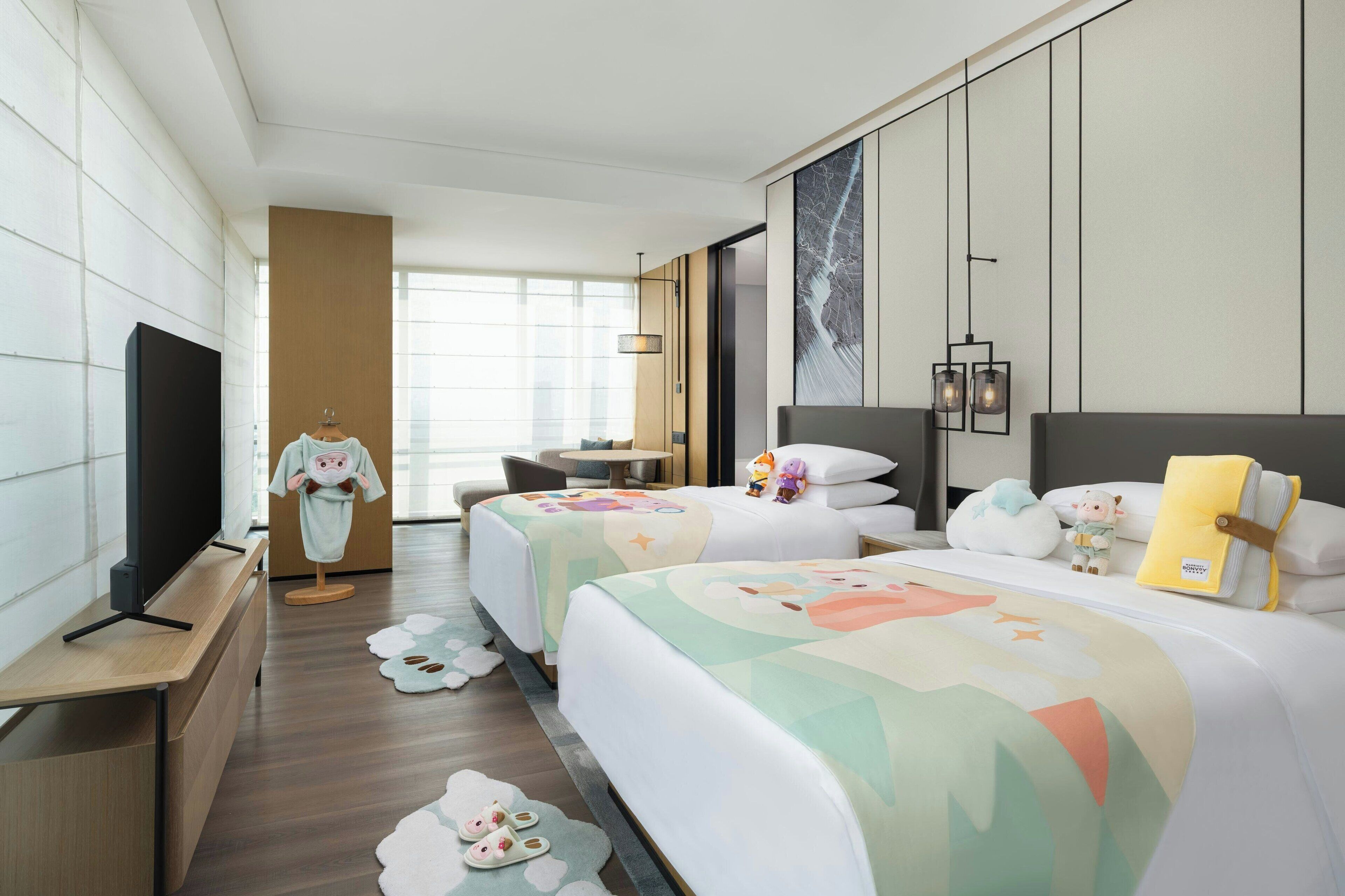 Quarto de hotel com duas camas, televisão, secretária e vista para a cidade.