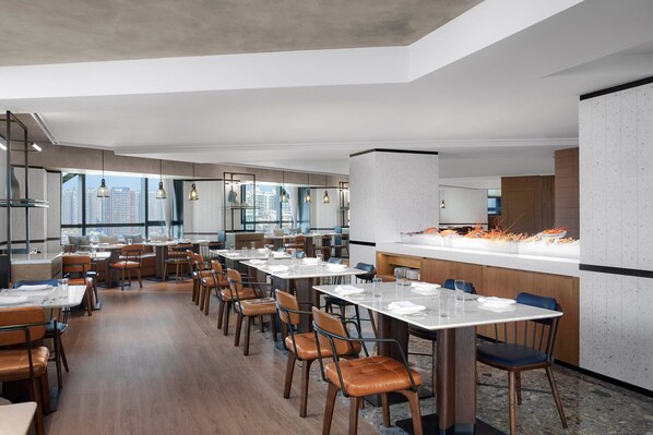 Um restaurante moderno com várias mesas e cadeiras, janelas amplas com vista para a cidade e um balcão com exposição de frutos do mar.