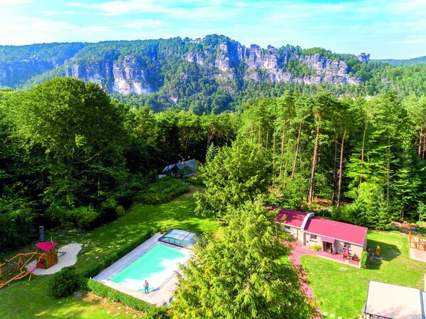 Uma casa com piscina cercada por vegetação exuberante e uma montanha arborizada ao fundo.