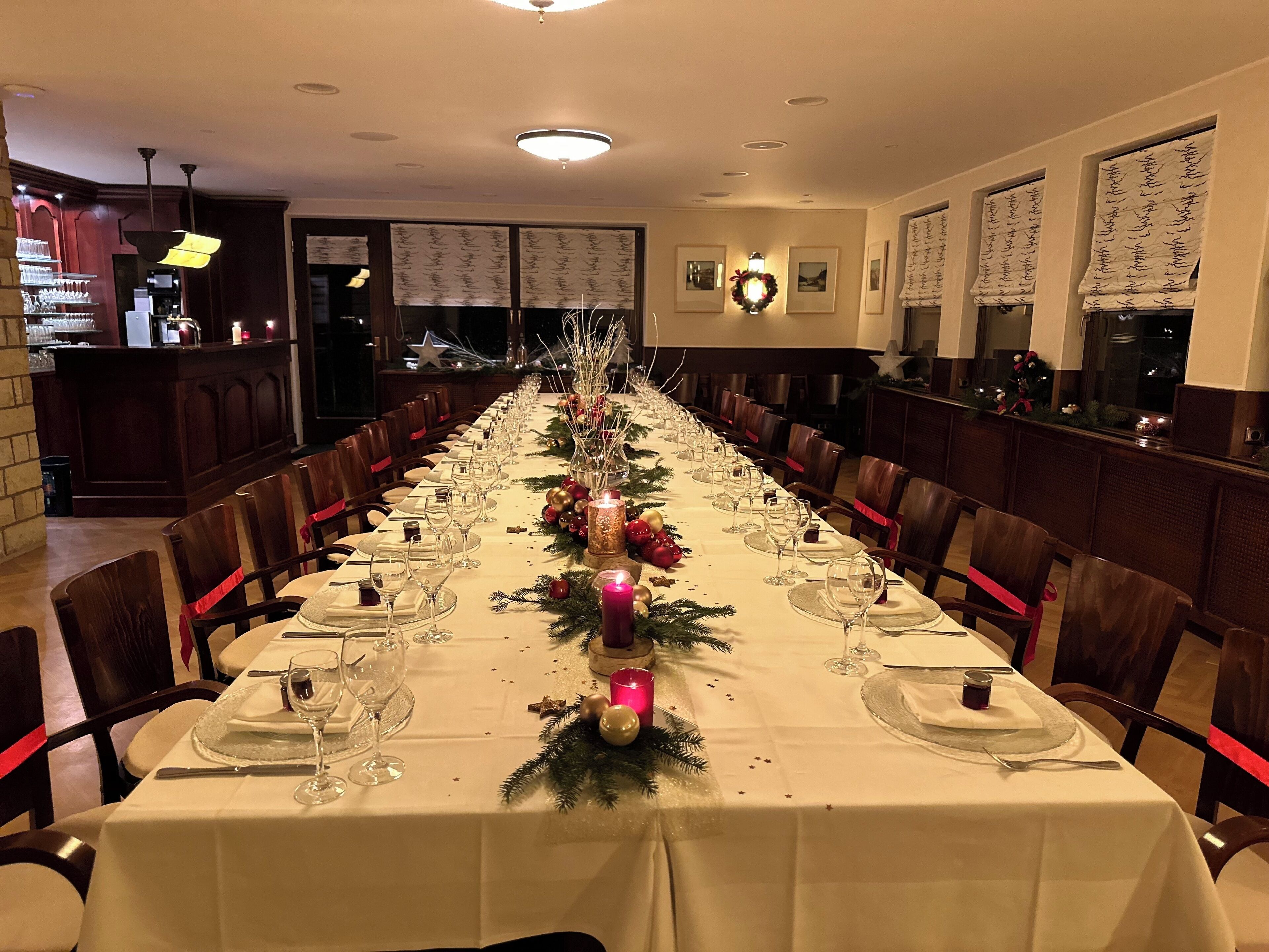 Mesa de jantar comprida posta com toalhas brancas, velas e decorações de Natal.