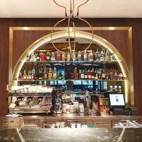 Uma área de bar com diversos frascos de bebidas, uma máquina de café e um caixa registradora.