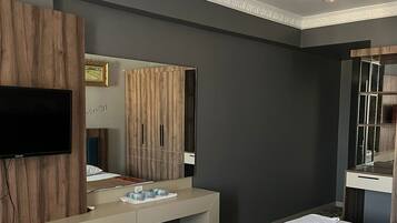 Quarto de hotel com duas camas, uma televisão, um espelho, uma escrivaninha de madeira e um ventilador de teto.