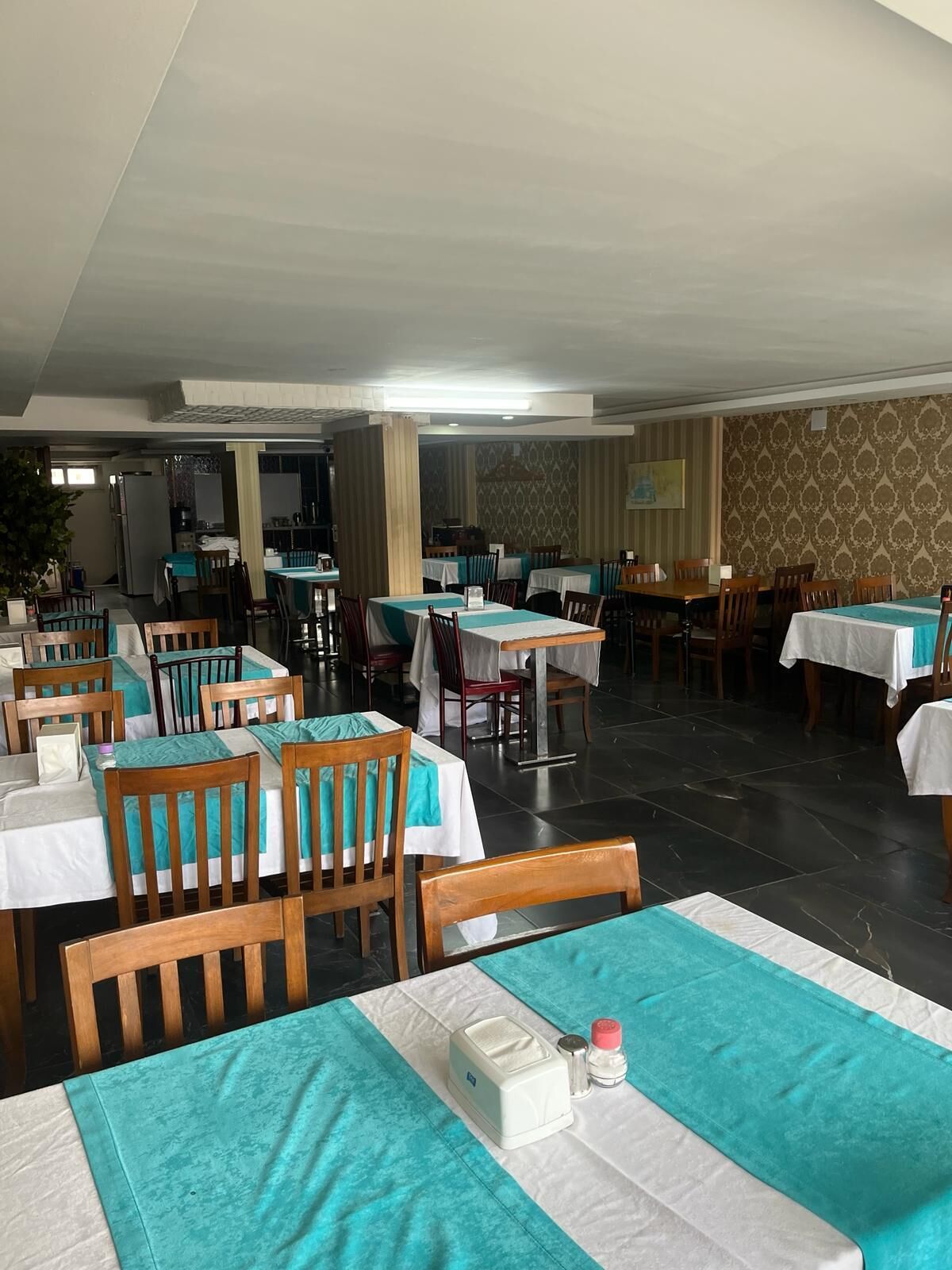 Um restaurante com várias mesas e cadeiras, algumas com toalhas de mesa cor turquesa.