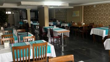 Um restaurante com várias mesas e cadeiras, algumas com toalhas de mesa cor turquesa.