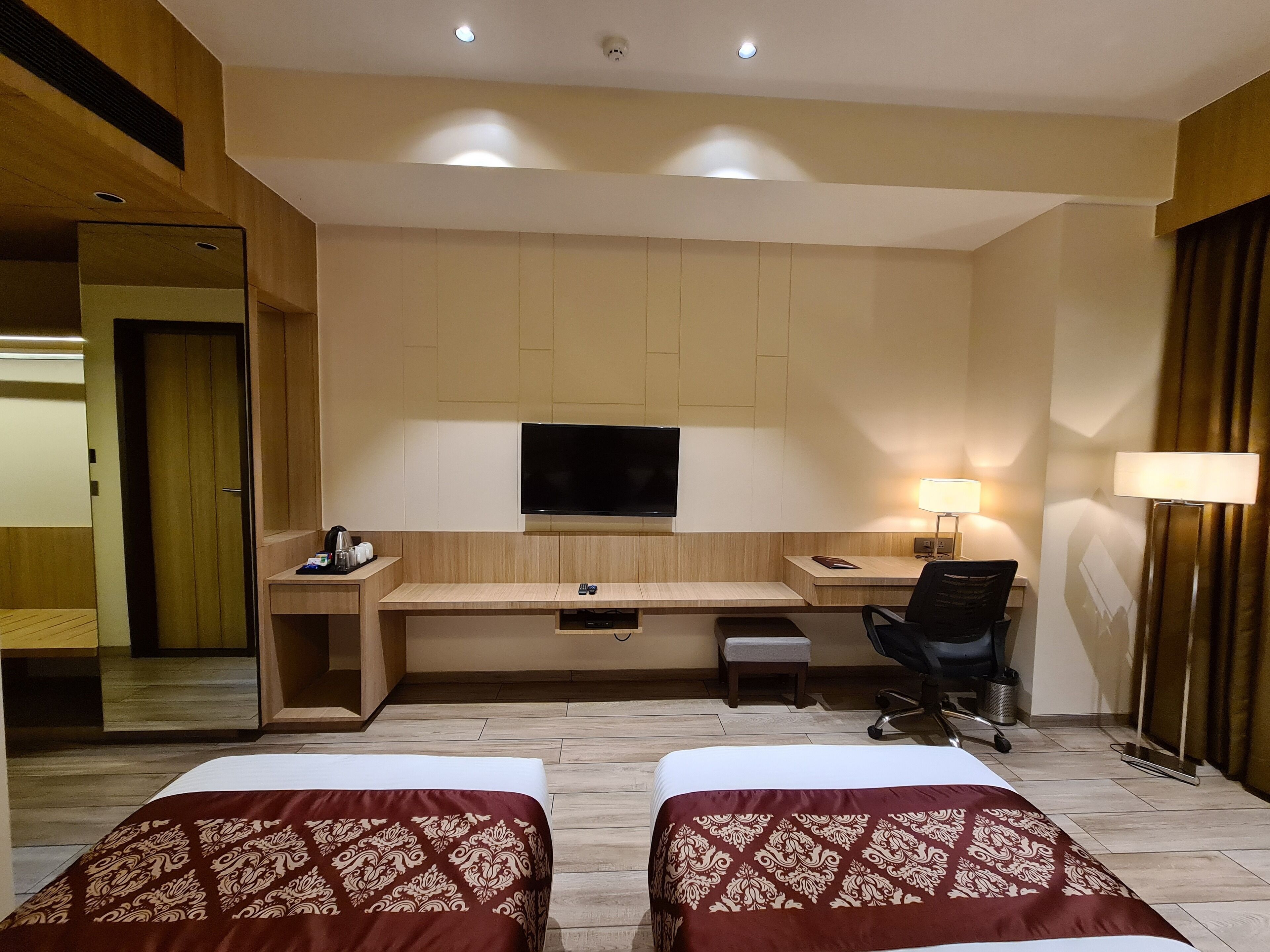 Quarto de hotel com duas camas, uma mesa de trabalho com cadeira, televisão e abajur.
