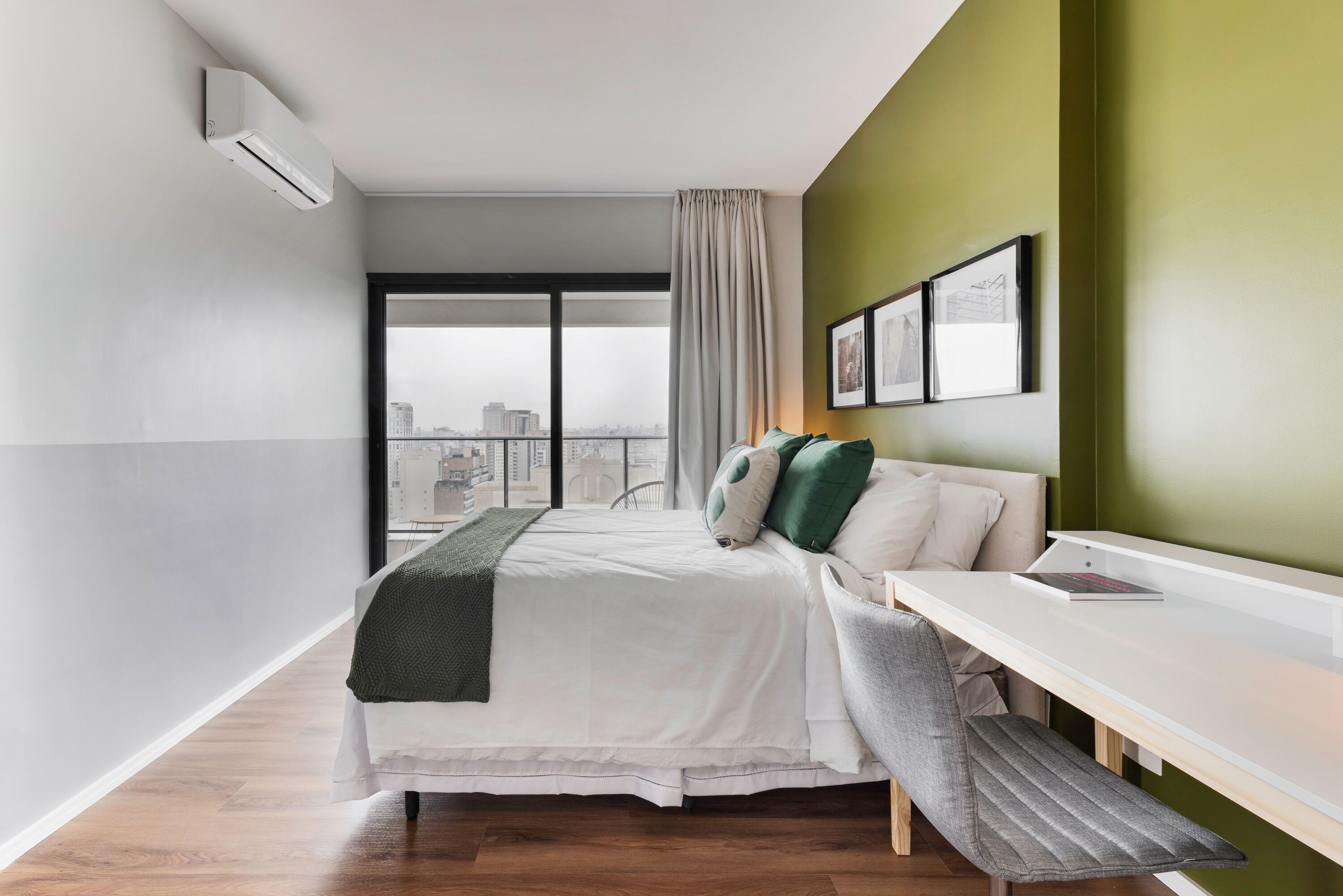 Quarto moderno com cama, escrivaninha e vista para a cidade.