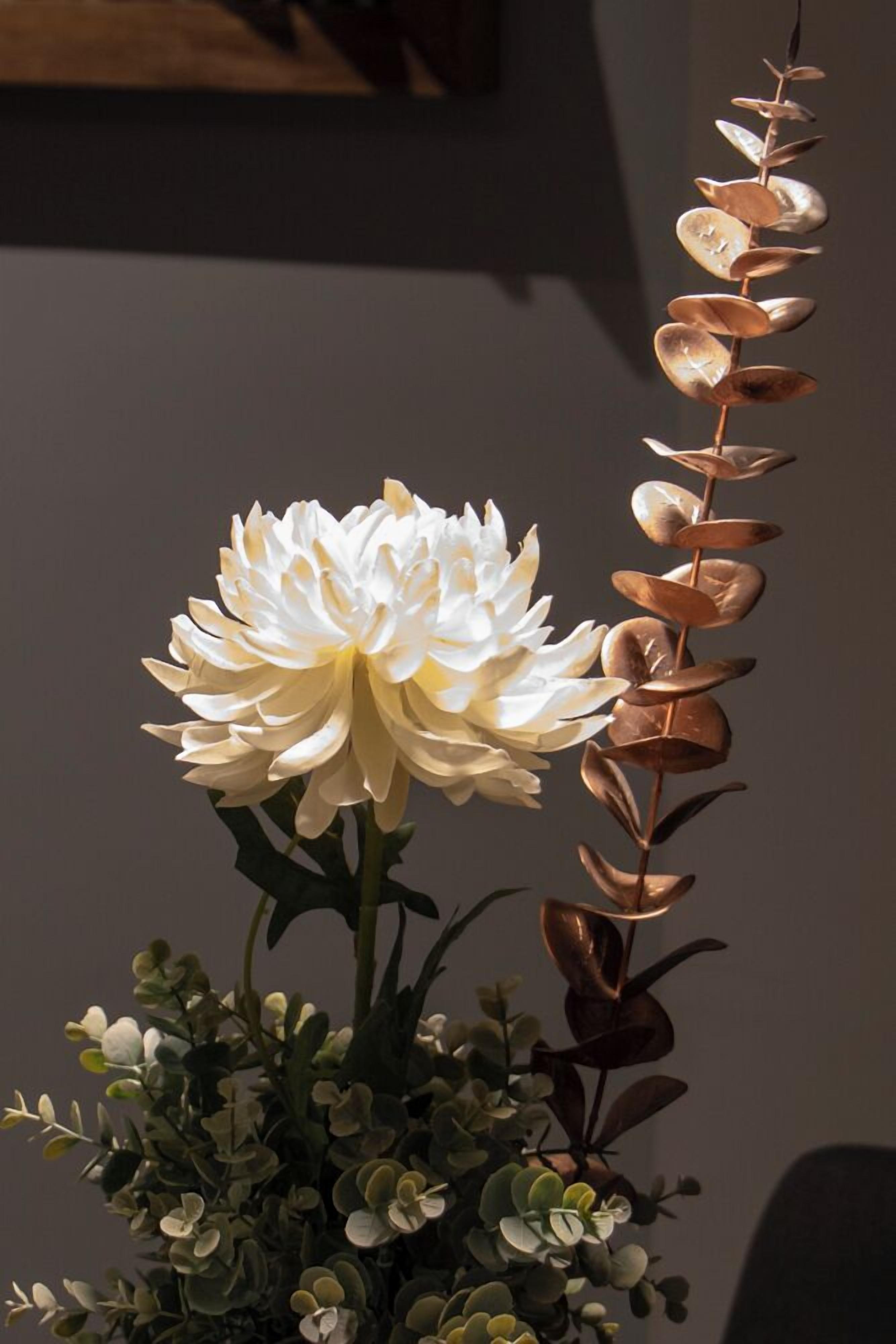 Uma flor branca num vaso com um detalhe decorativo cor de cobre.