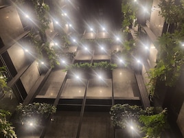 Um átrio moderno com um espaço aberto central, rodeado por paredes com jardineiras e luminárias integradas.