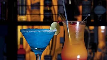 Dois cocktails em um balcão de bar com uma variedade de garrafas ao fundo.