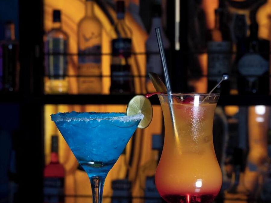 Dois cocktails em um balcão de bar com uma variedade de garrafas ao fundo.