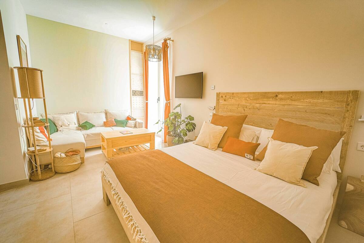 Um quarto com uma cama grande, um sofá, uma mesinha e um vaso de planta.