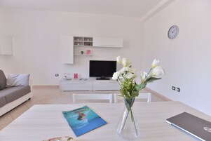 Uma sala de estar moderna com um sofá branco, uma mesa de jantar com um vaso de flores, um livro e um laptop.