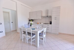 Uma cozinha moderna com armários brancos, uma mesa de jantar com cadeiras e piso ladrilhado.