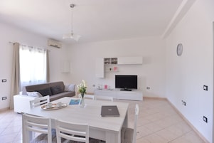 Uma sala de estar moderna com área de refeições, sofá, TV e um laptop sobre a mesa.