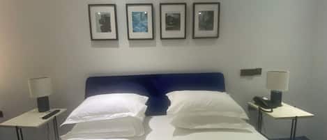 Quarto de hotel com uma cama grande, duas mesas de cabeceira, um criado-mudo e um telefone fixado na parede.