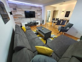 Uma sala de estar moderna com parede de pedra, televisão de tela plana, conjunto de sofá, mesa de centro e área de jantar com cadeiras e mesa.
