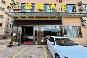 Entrada de hotel com um carro estacionado em frente, um tapete vermelho levando à porta e uma placa sobre a entrada.