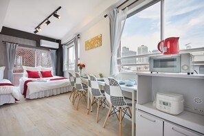 Quarto de hotel moderno com vista para a cidade, área de refeições com cadeiras estampadas, micro-ondas e chaleira no balcão.