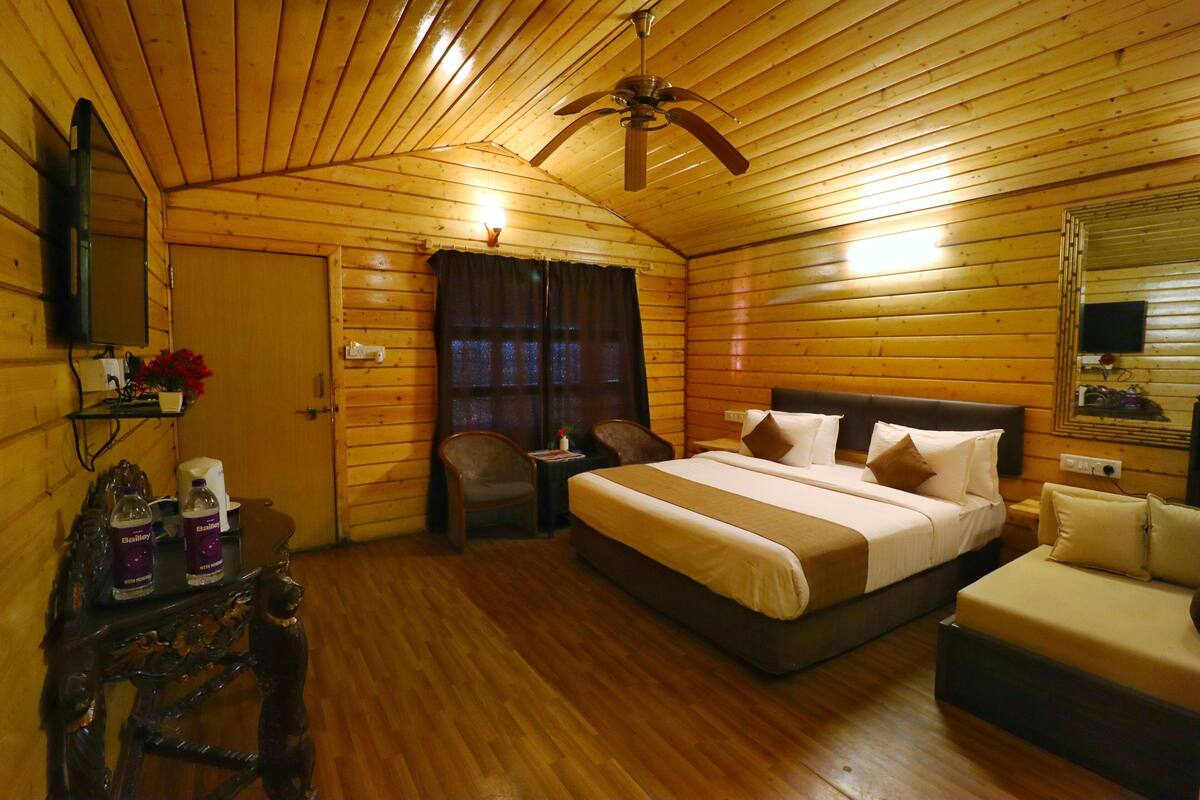 Quarto com painéis de madeira, uma cama grande, um sofá menor, uma escrivaninha com cadeira e um ventilador de teto.