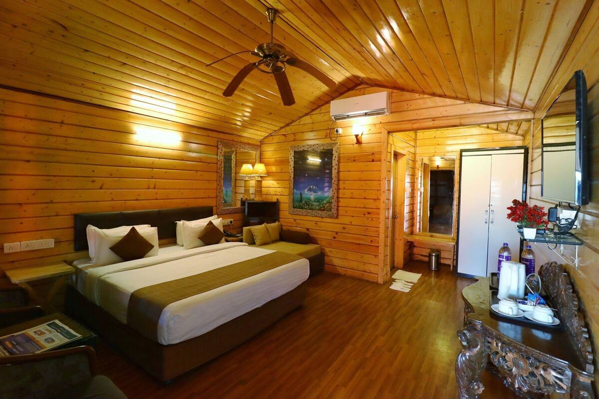 Uma cabana de madeira com uma cama, uma escrivaninha, uma cadeira, um espelho, uma televisão e um chuveiro.