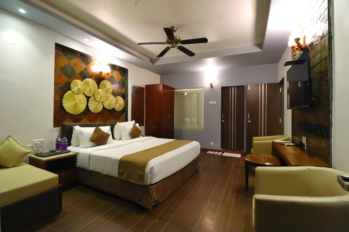 Quarto de hotel com uma cama grande, um ventilador de teto, uma TV fixada na parede e uma área de estar com mesa e cadeiras.