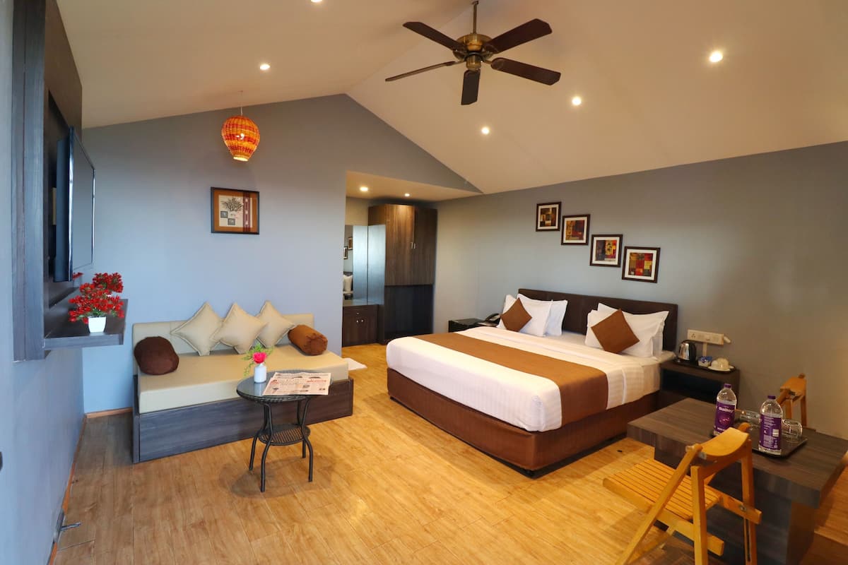 Quarto de hotel moderno com uma cama grande, um sofá, uma mesa pequena e um ventilador de teto.