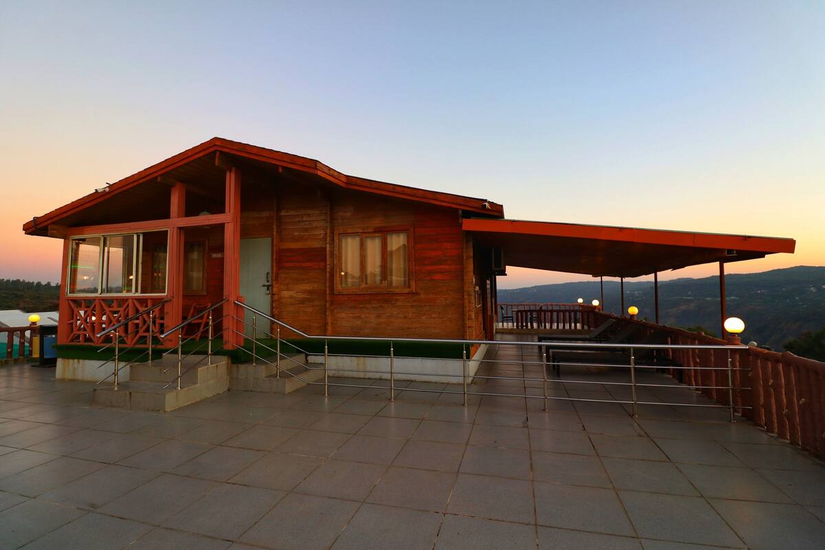 Uma cabana de madeira com varanda, escadas e vista para a paisagem.
