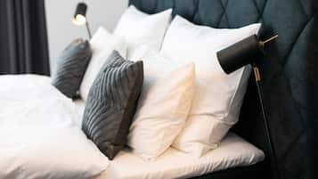 Uma cama bem arrumada com almofadas brancas e cinzentas, uma cabeceira preta e um abajur.