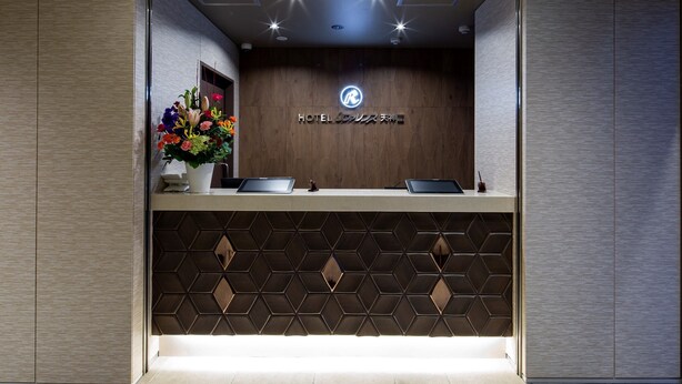 Uma receção de hotel com design moderno, exibindo um logótipo, um ecrã digital e um arranjo floral.