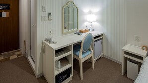 Quarto de hotel com escrivaninha, cadeira, mesa de cabeceira e uma pequena luminária.