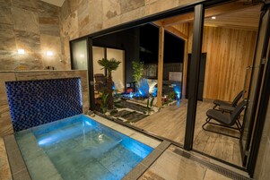 Uma área interna de piscina moderna, com uma seção envidraçada, parede revestida de azulejos azuis e um deck de madeira com um banco.