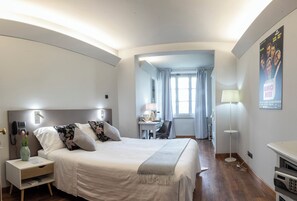 Quarto de hotel moderno com cama grande, mesa de cabeceira, abajur e escrivaninha com cadeira.