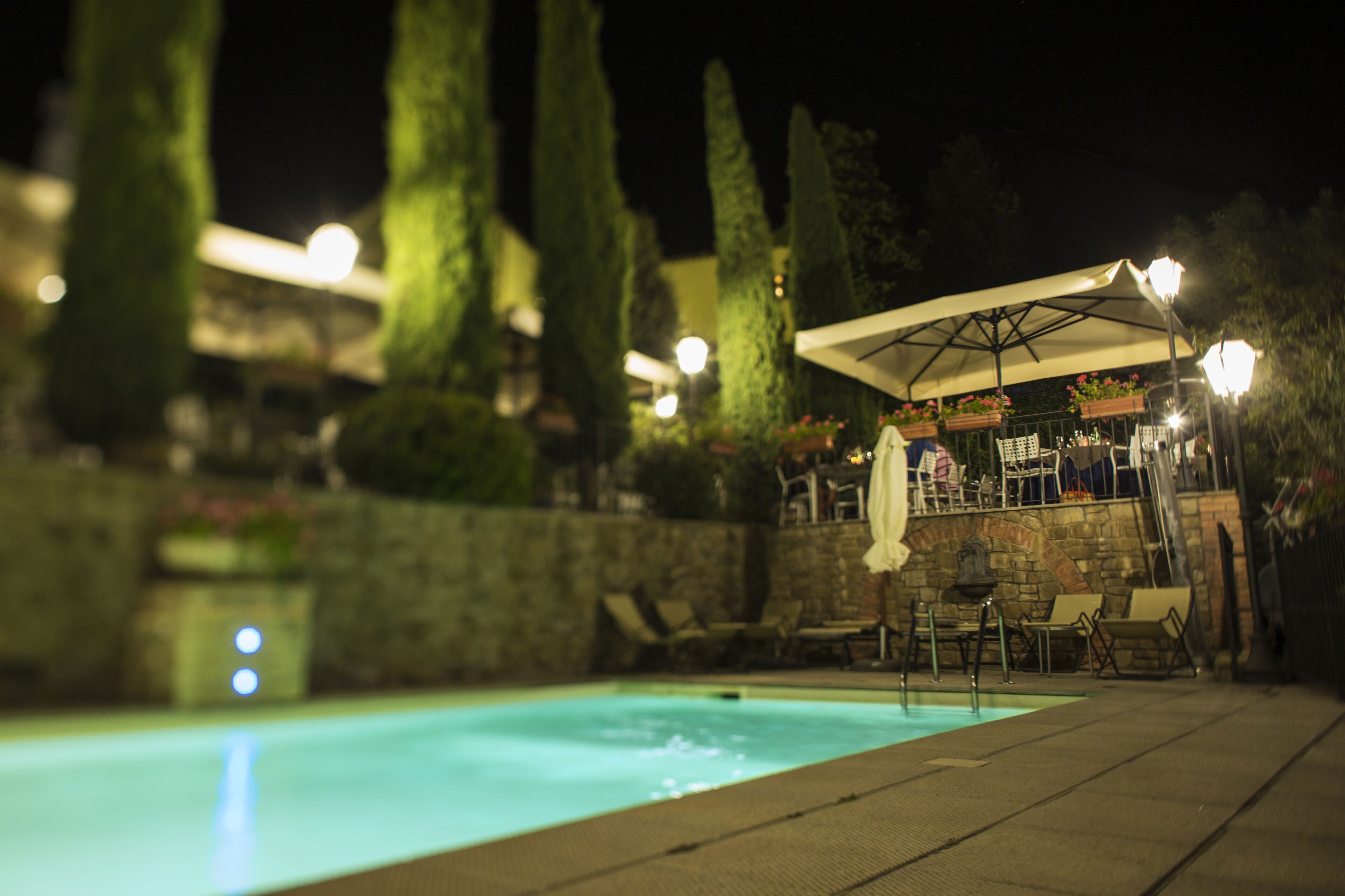 Uma área de piscina ao ar livre à noite, com parede de pedra, espreguiçadeiras e um toldo.