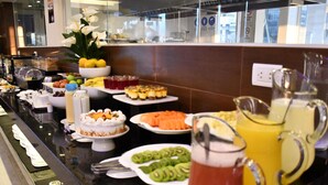 Buffet com diversos tipos de comida e um jarro de suco de laranja.