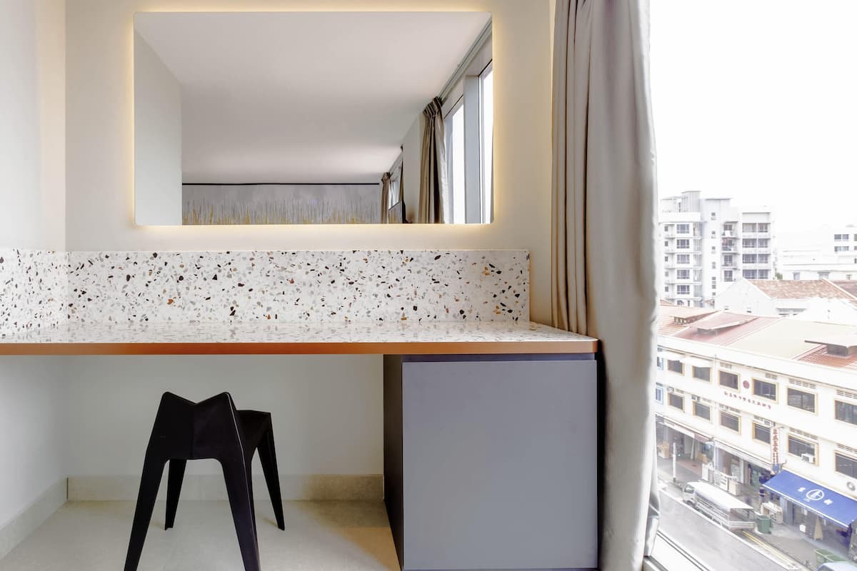 Quarto moderno com escrivaninha, cadeira e vista para a cidade pela janela.