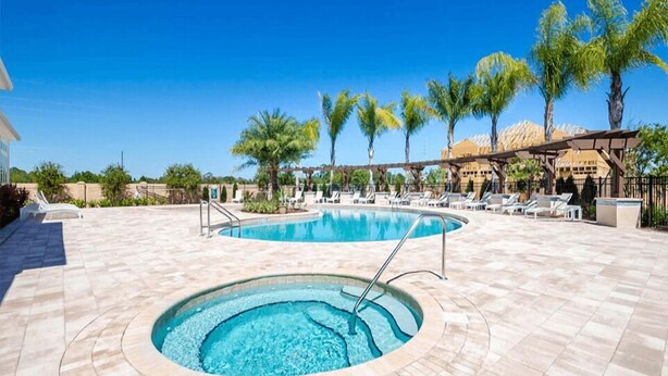 Uma área de piscina com duas piscinas, espreguiçadeiras, palmeiras e um pérgola.