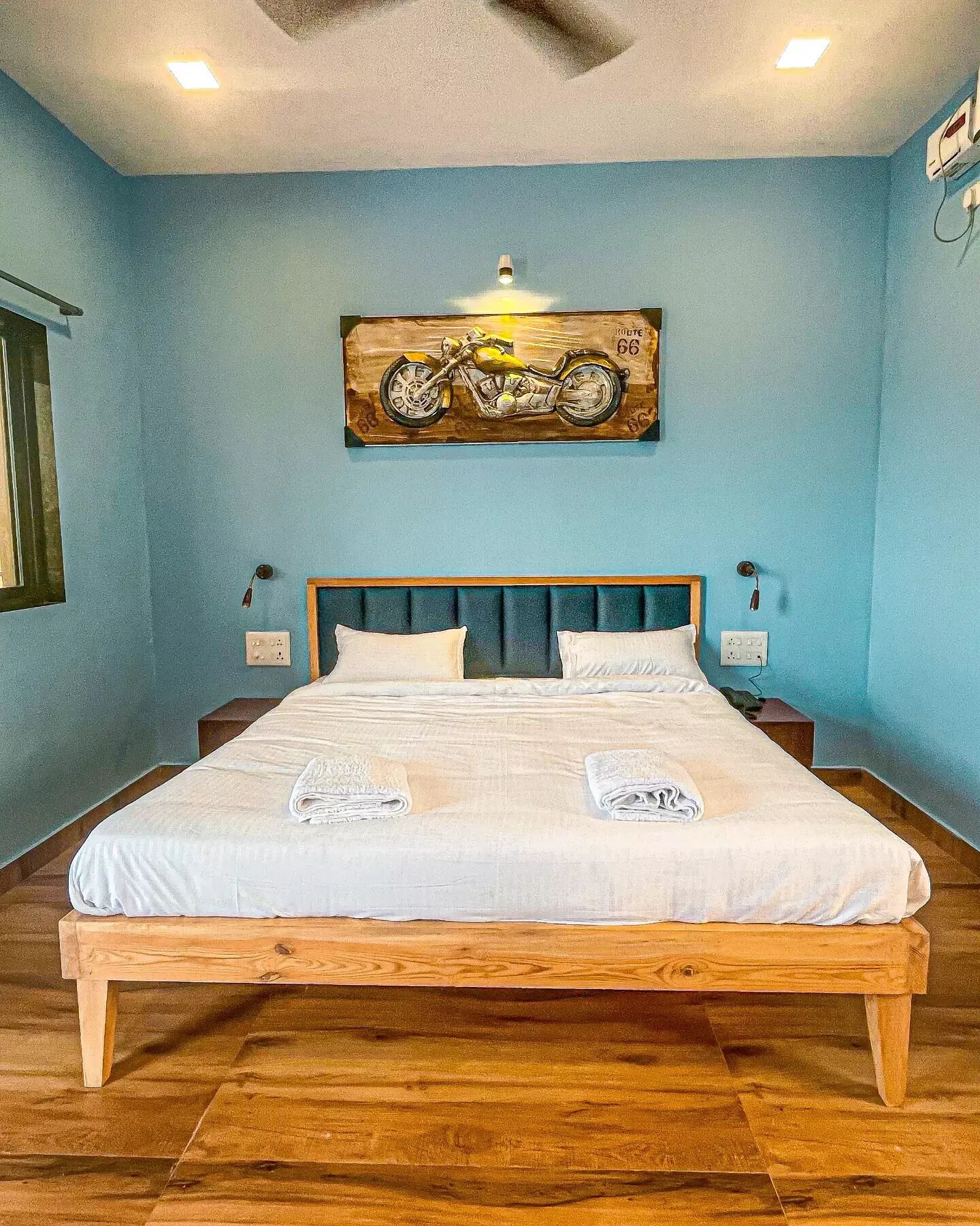 Quarto com cama grande, cabeceira de madeira e um quadro de uma moto na parede.
